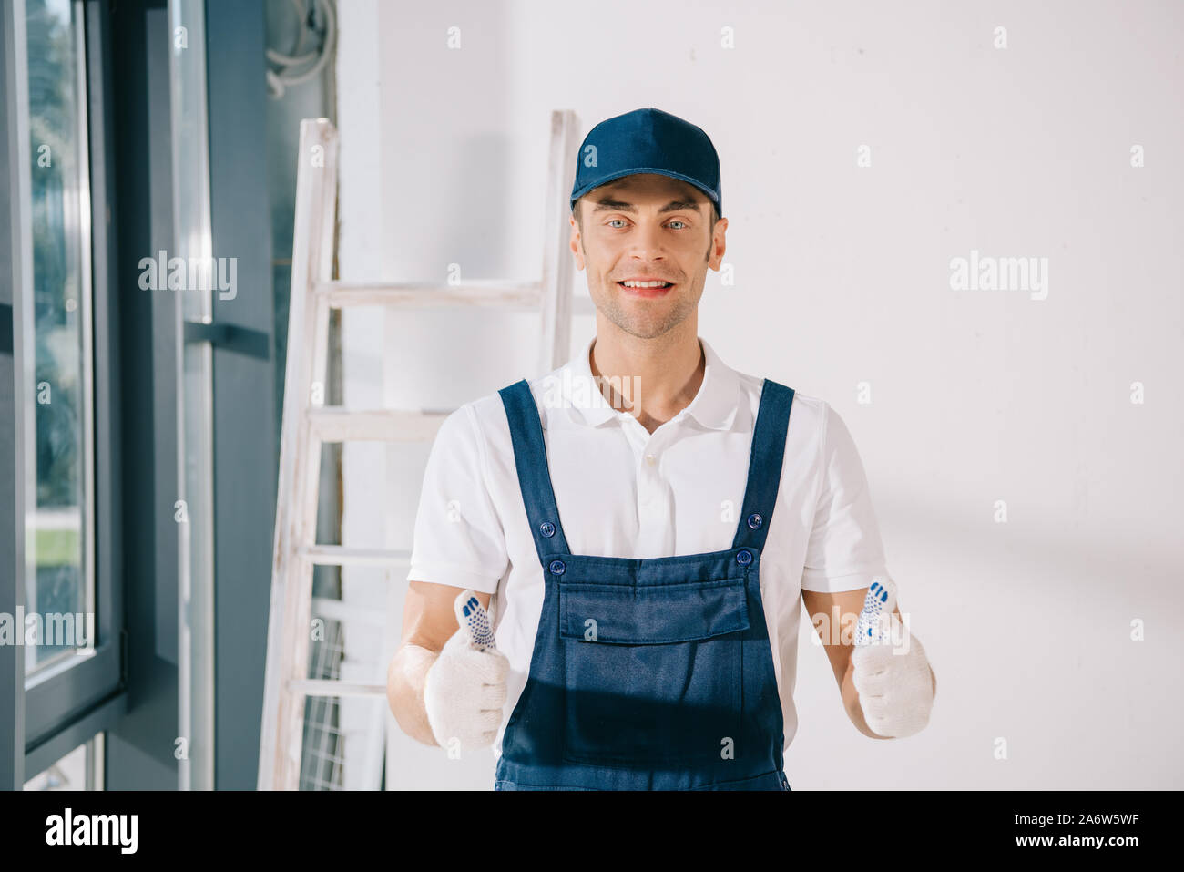 handsome painter in uniform showing thumbs up and smiling at camera ...
