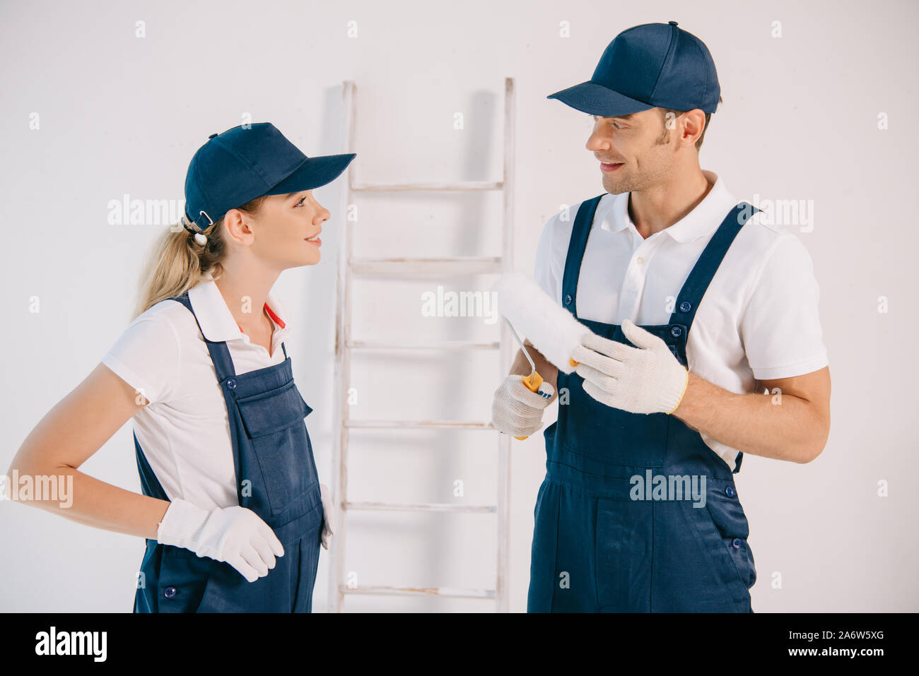 handsome painter in uniform holding paint roller while talking with ...