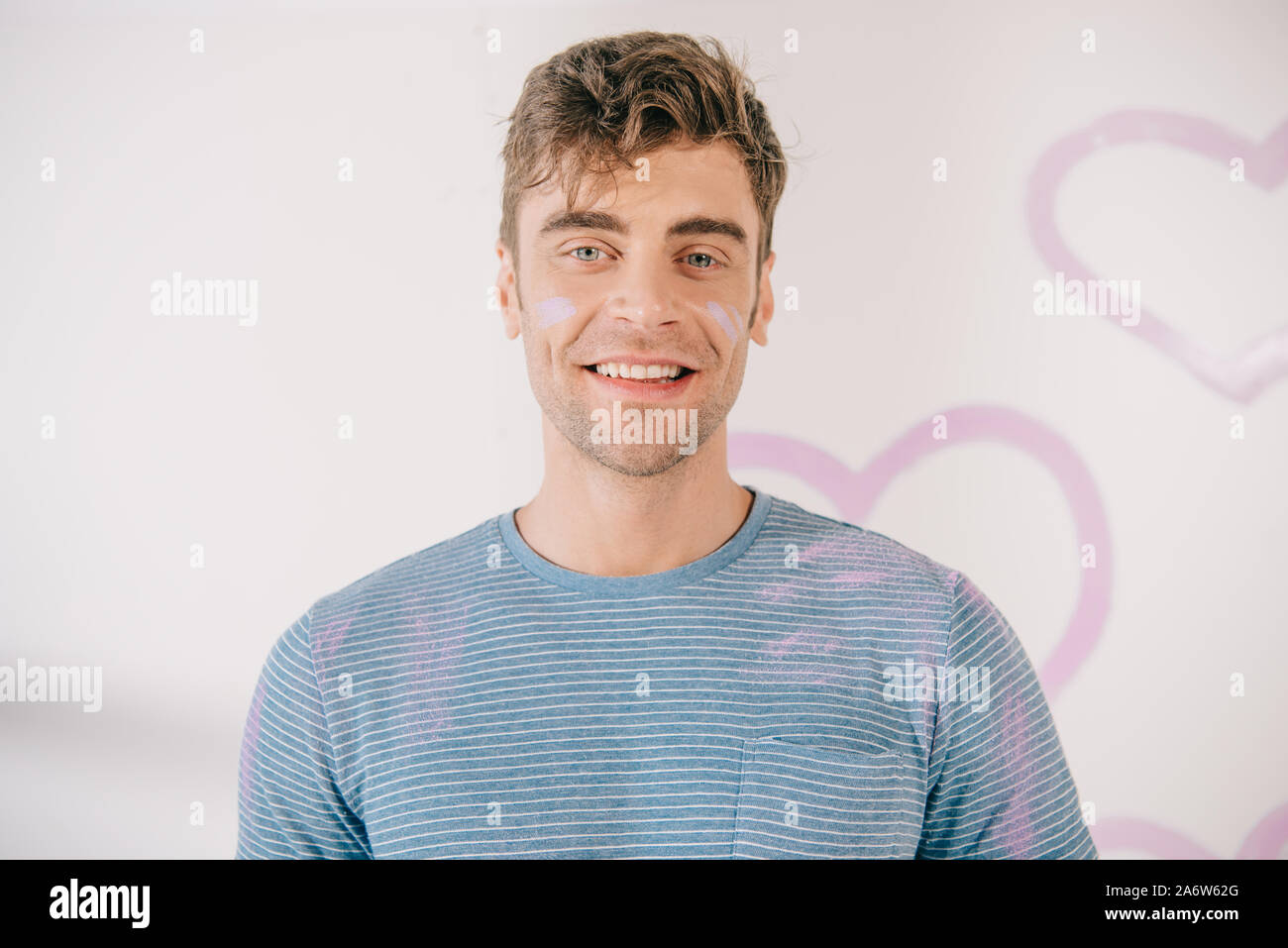 handsome young man with stains of pink paint on face looking at camera ...