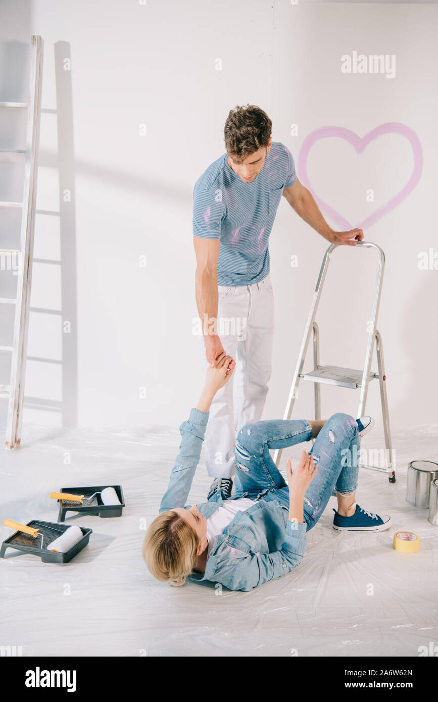 young man helping girlfriend fallen from ladder and lying on floor ...