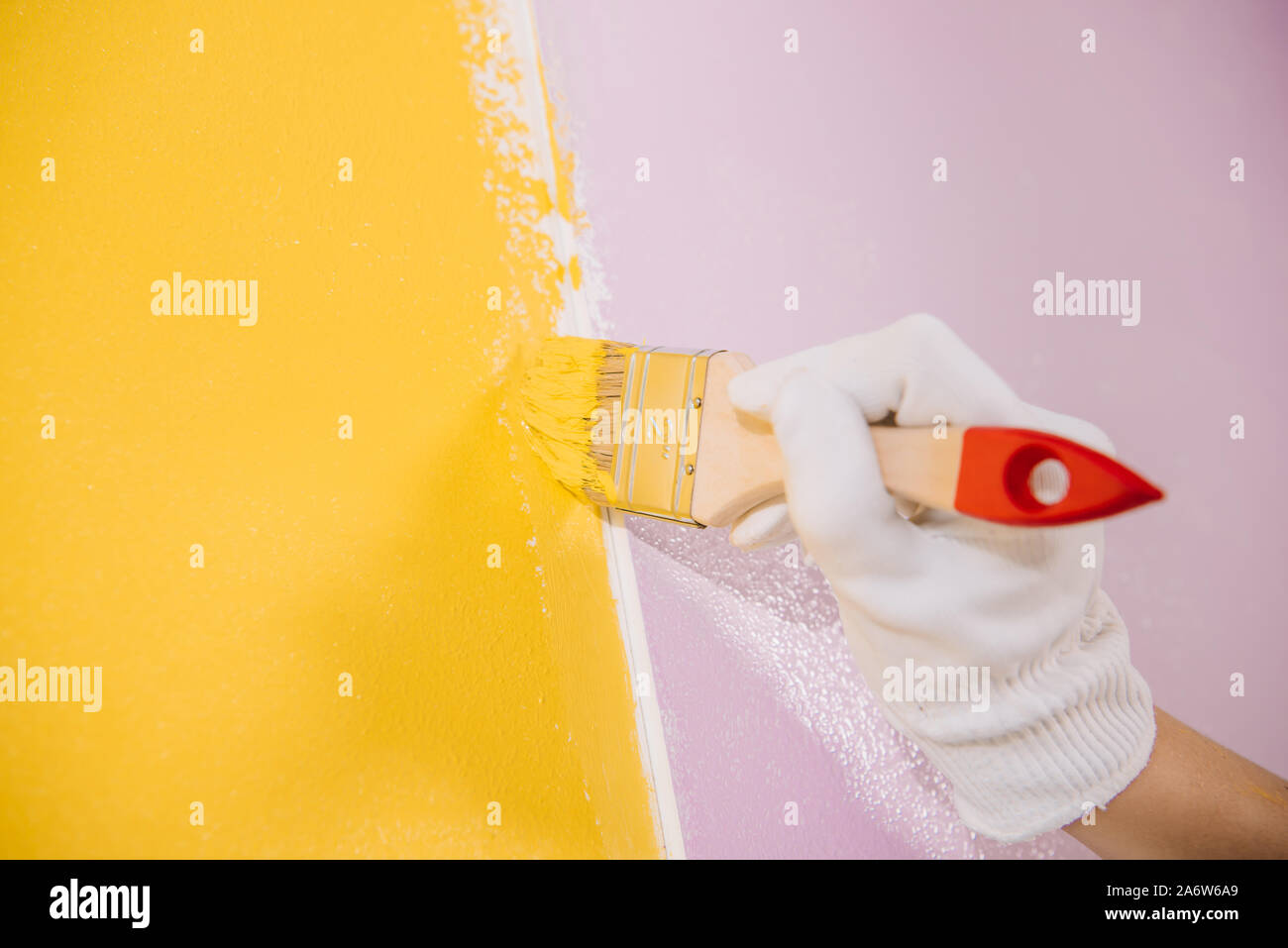 partial view of painter painting wall in yellow and pink with ...