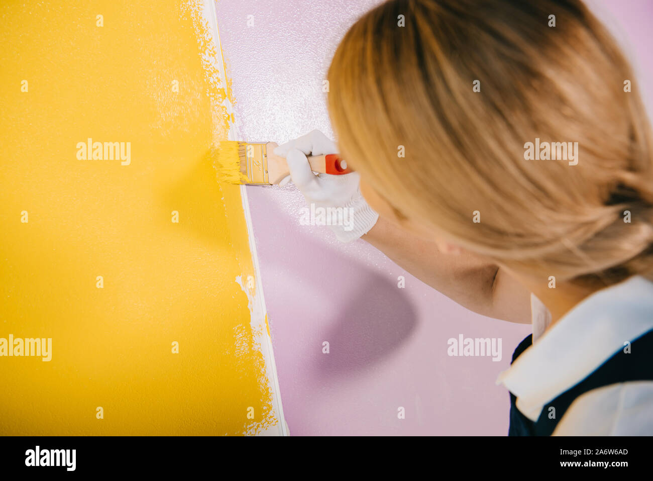 back view of young painter painting wall in yellow and pink with ...