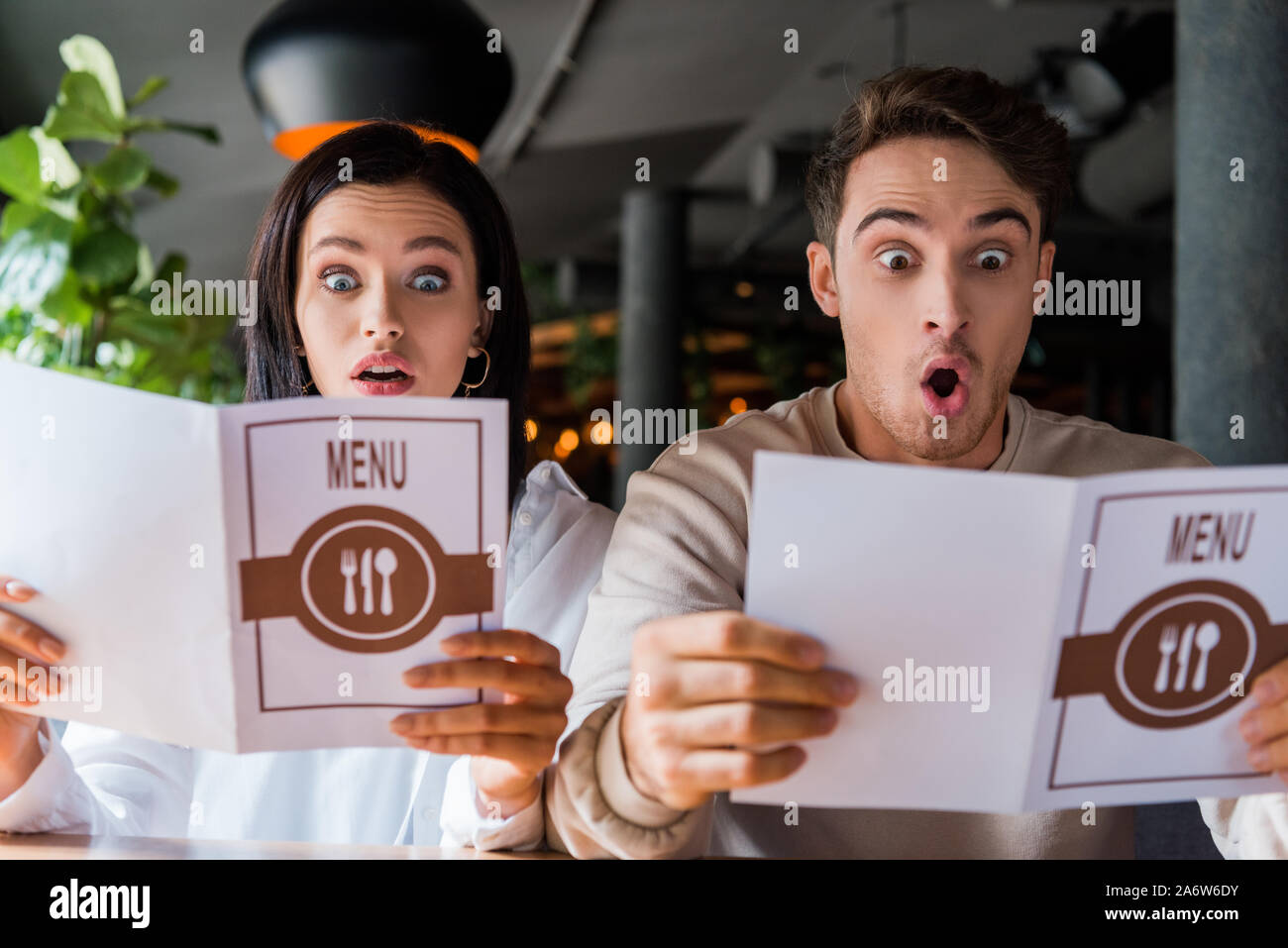 shocked man and woman looking at menus in restaurant Stock Photo - Alamy
