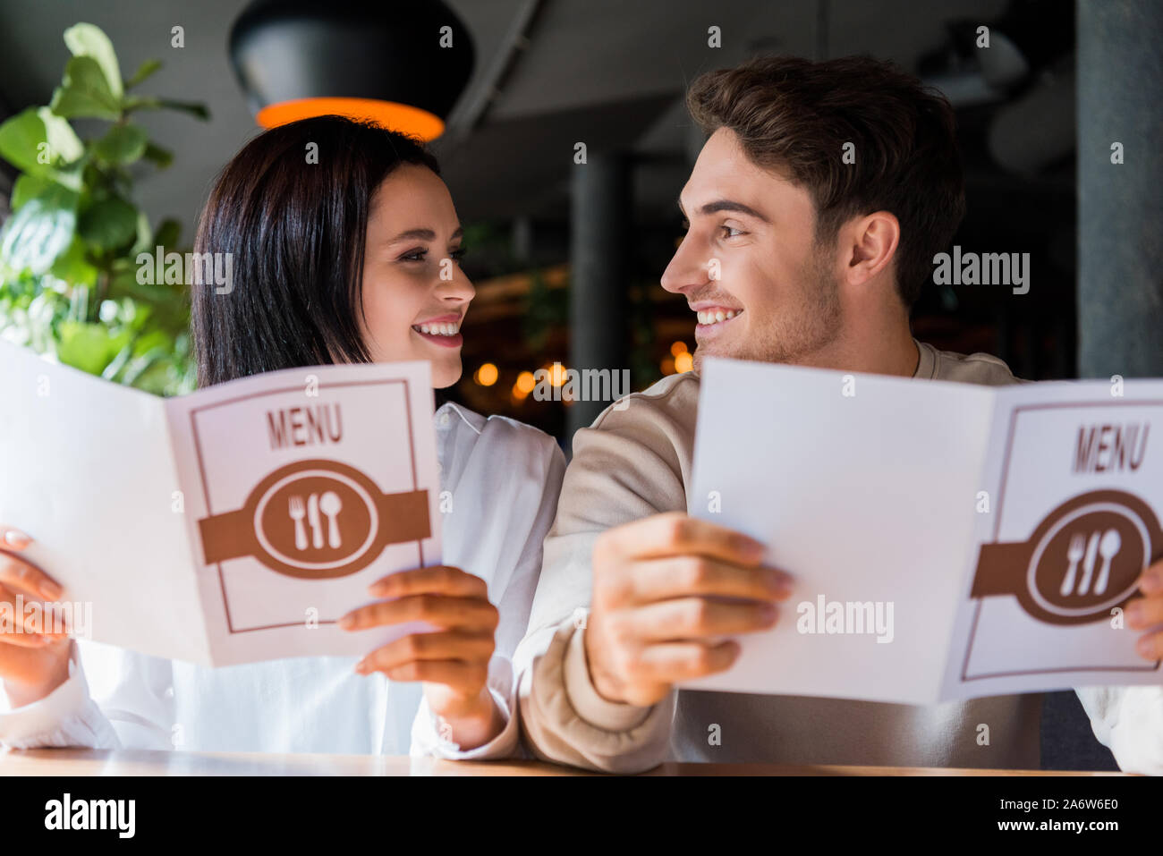 happy man and woman looking at each other while holding menus in ...