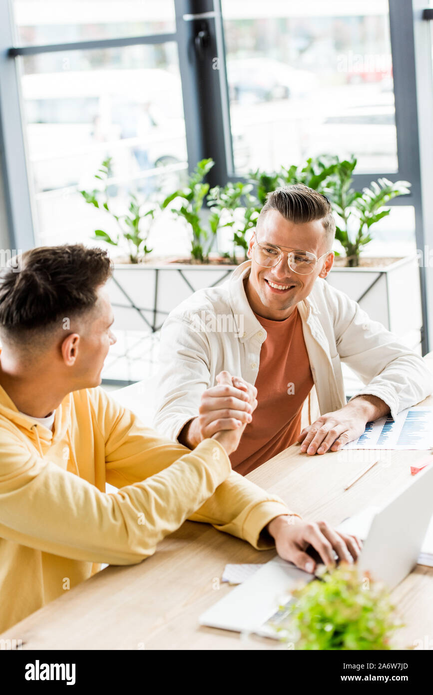 two young, handsome businessmen shaking hands while sitting together at ...