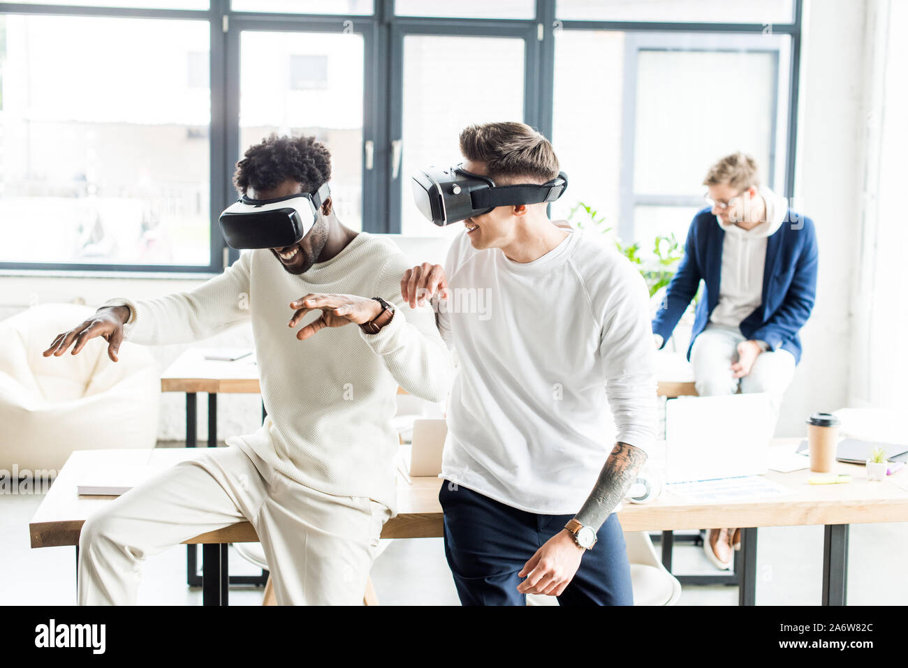two cheerful multicultural colleagues using vr headsets in office Stock ...