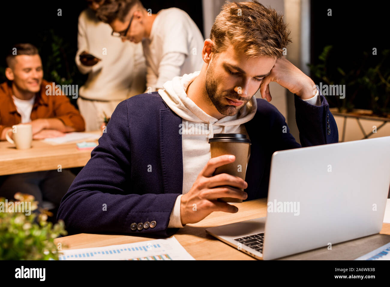 exhausted businessman holding coffee to go while working at night in ...