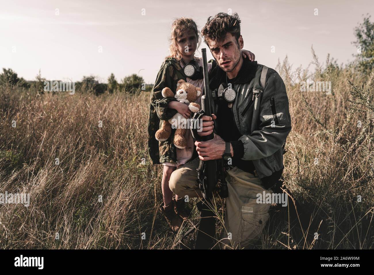 handsome man holding gun near cute kid with soft toy in field, post ...