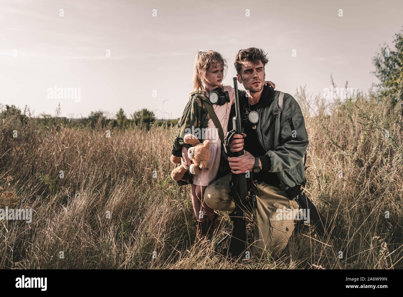 handsome man holding gun near kid with soft toy in field, post ...