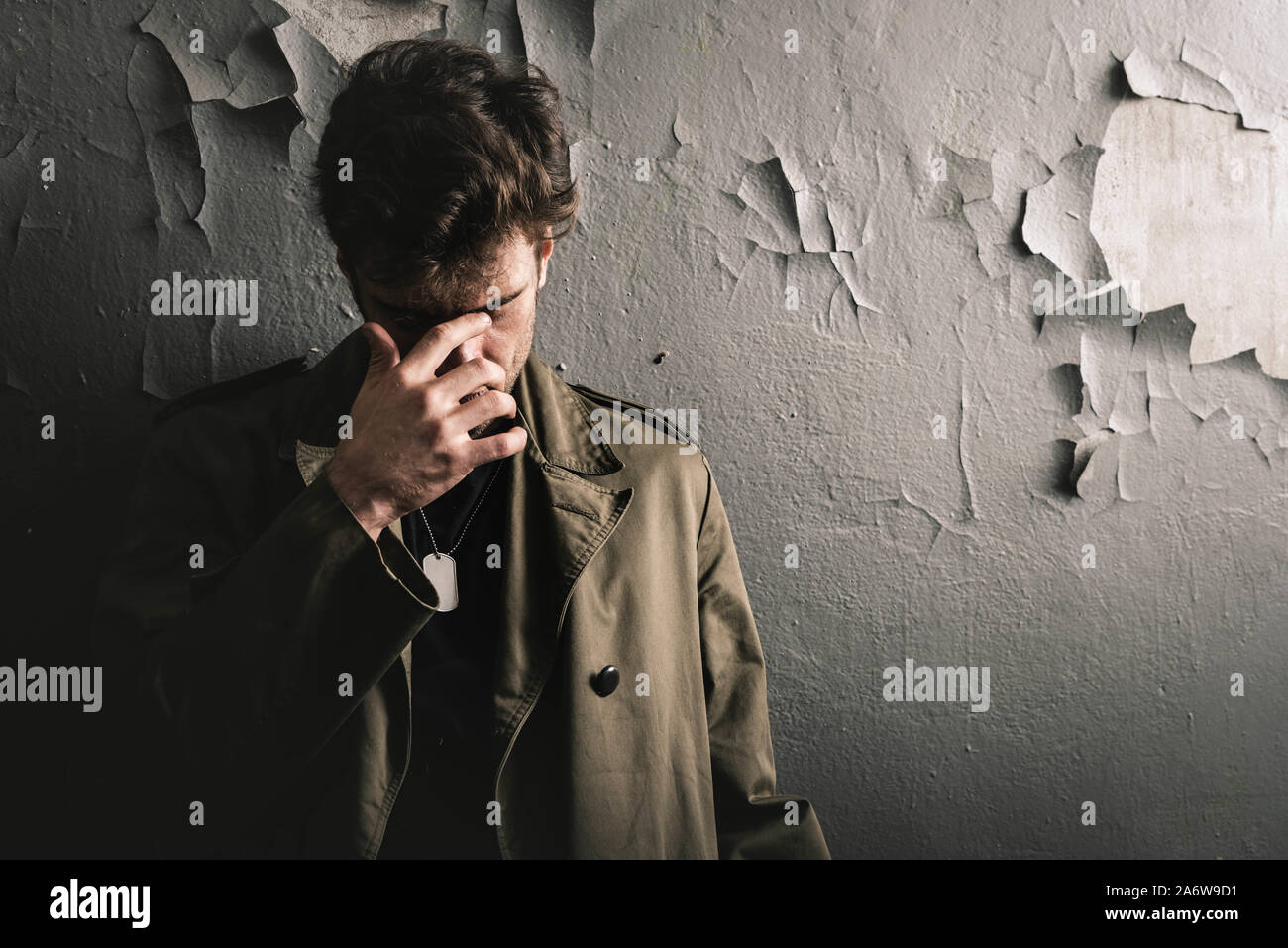 man touching face while standing near old wall, post apocalyptic ...