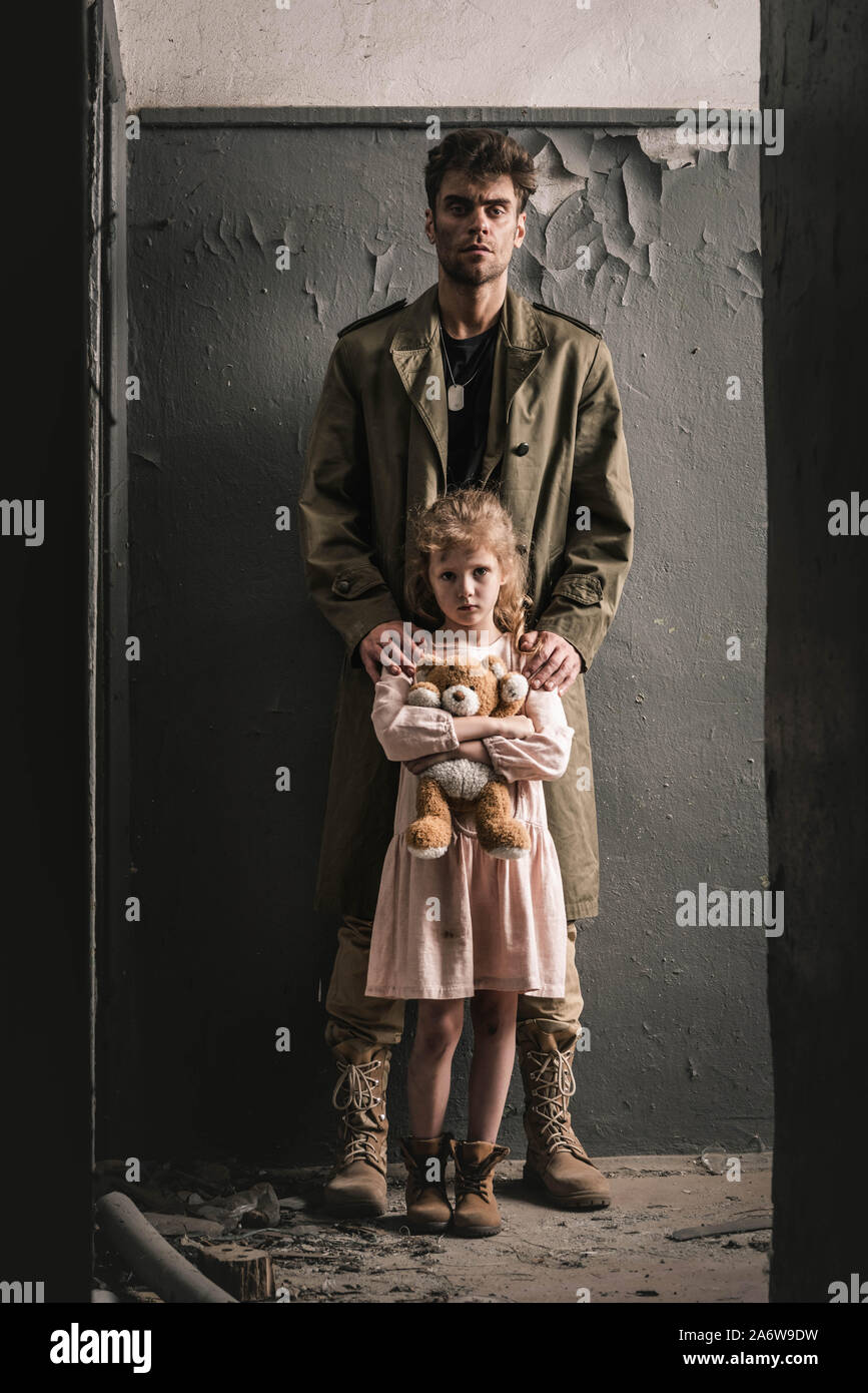 handsome man standing with kid holding teddy bear near weathered wall ...
