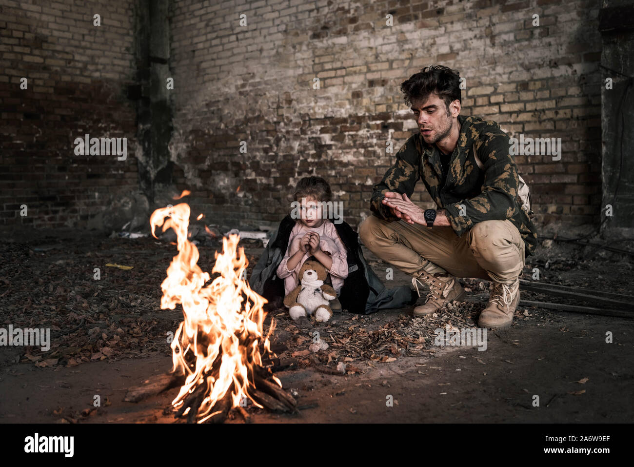 selective focus of man and child sitting near bonfire, post apocalyptic ...