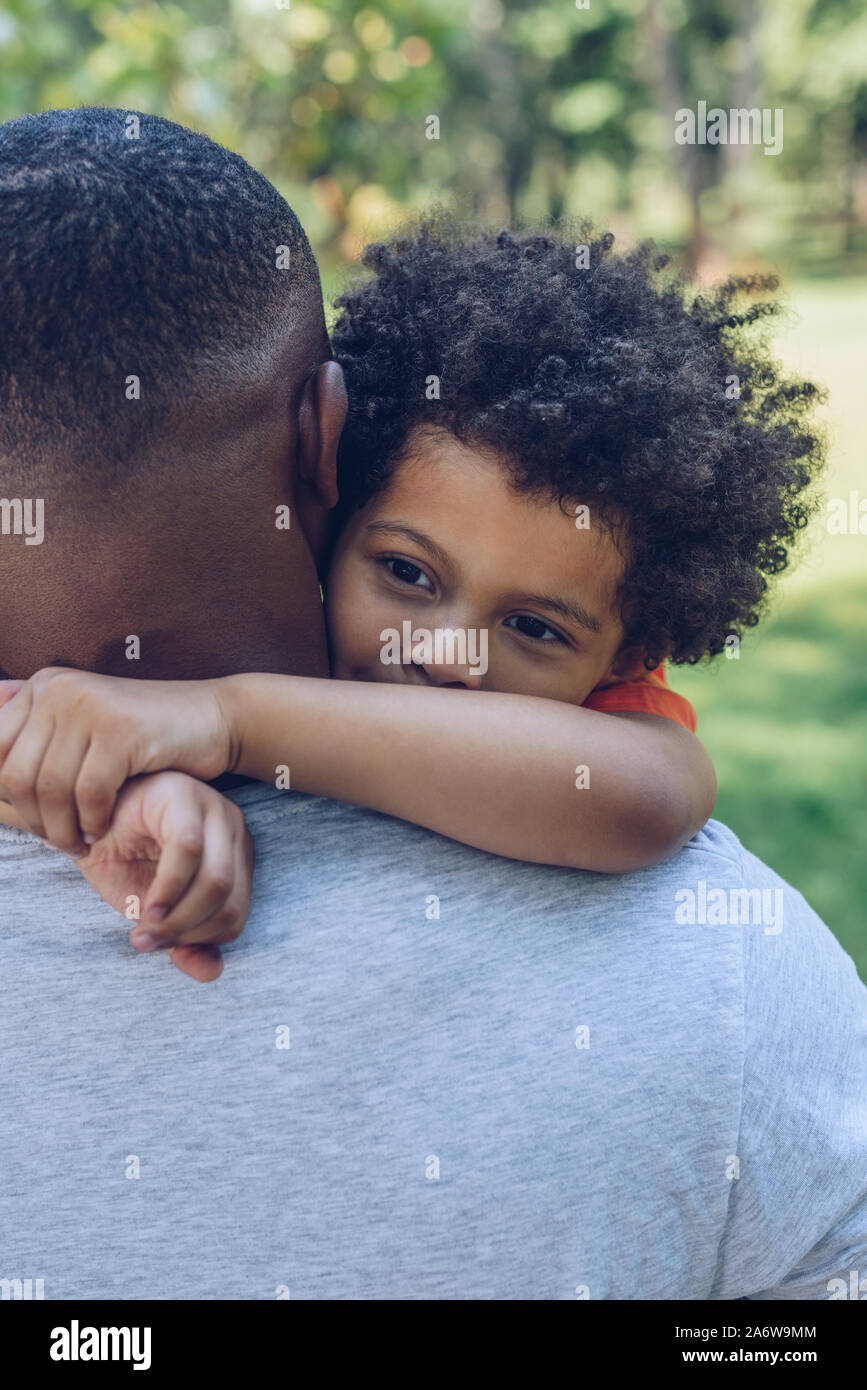 adorable african american boy hugging father while walking in park ...