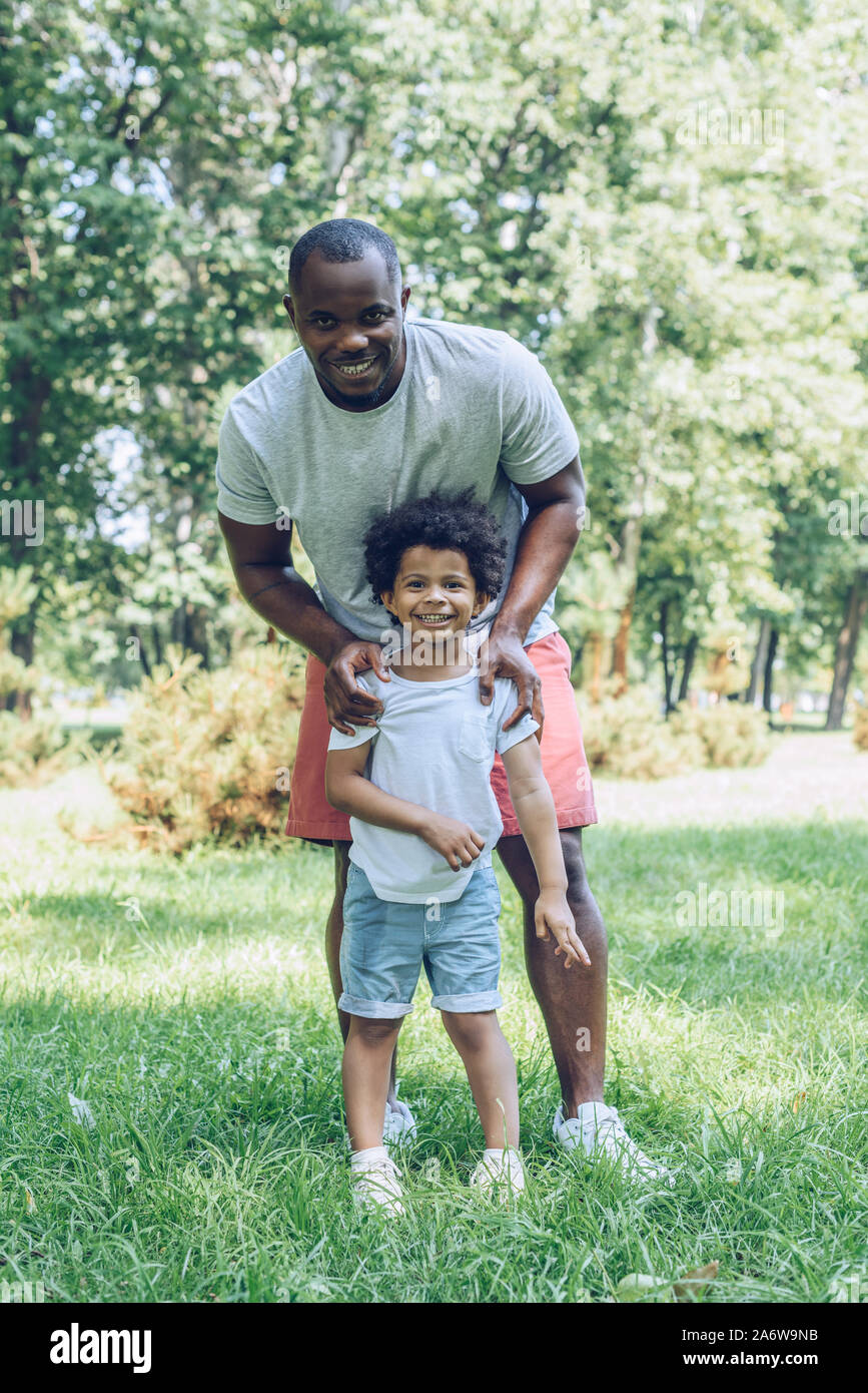 happy african american father and son smiling at camera while walking ...