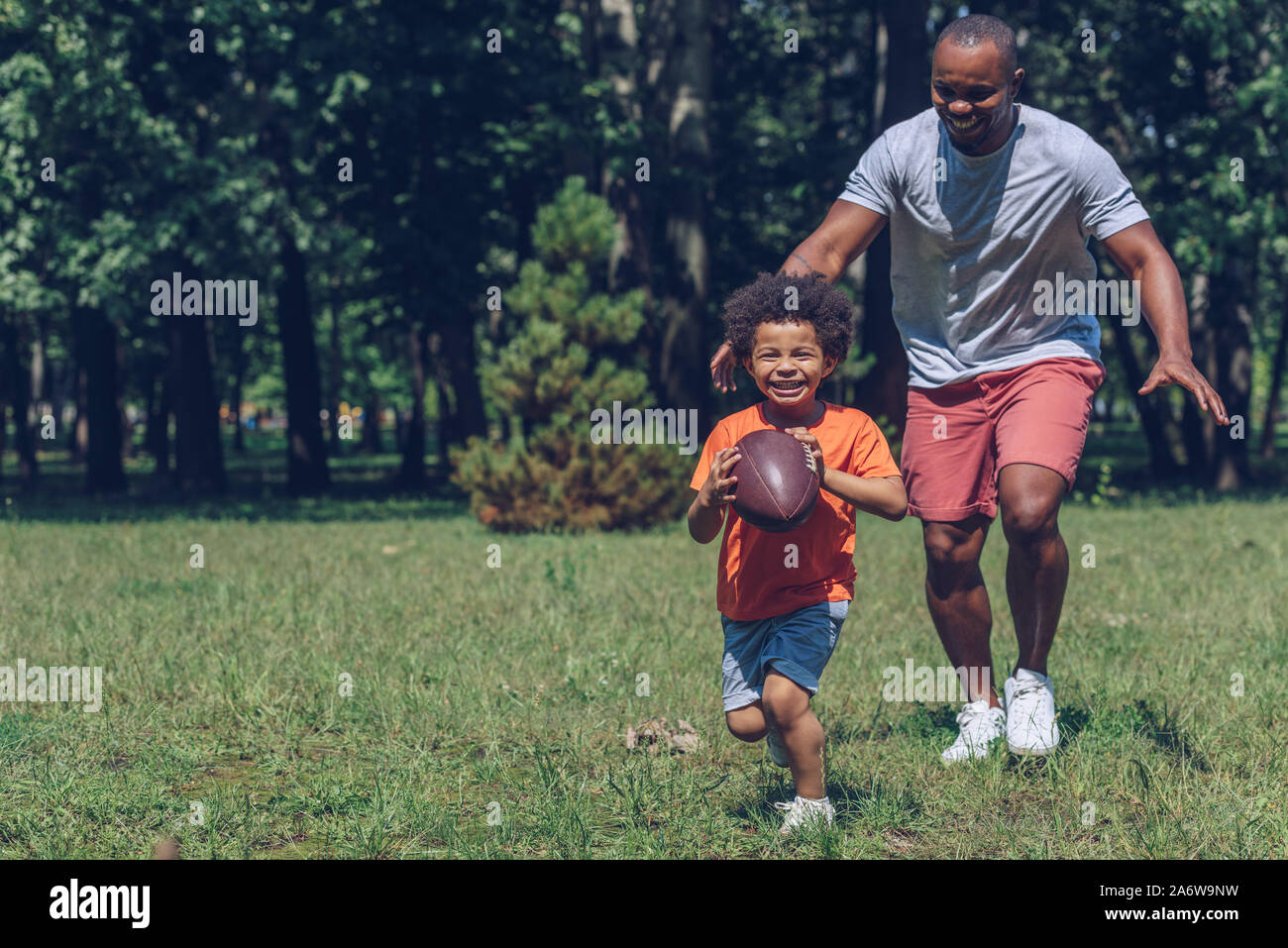 cute african american boy running with rugby ball while having fun with ...