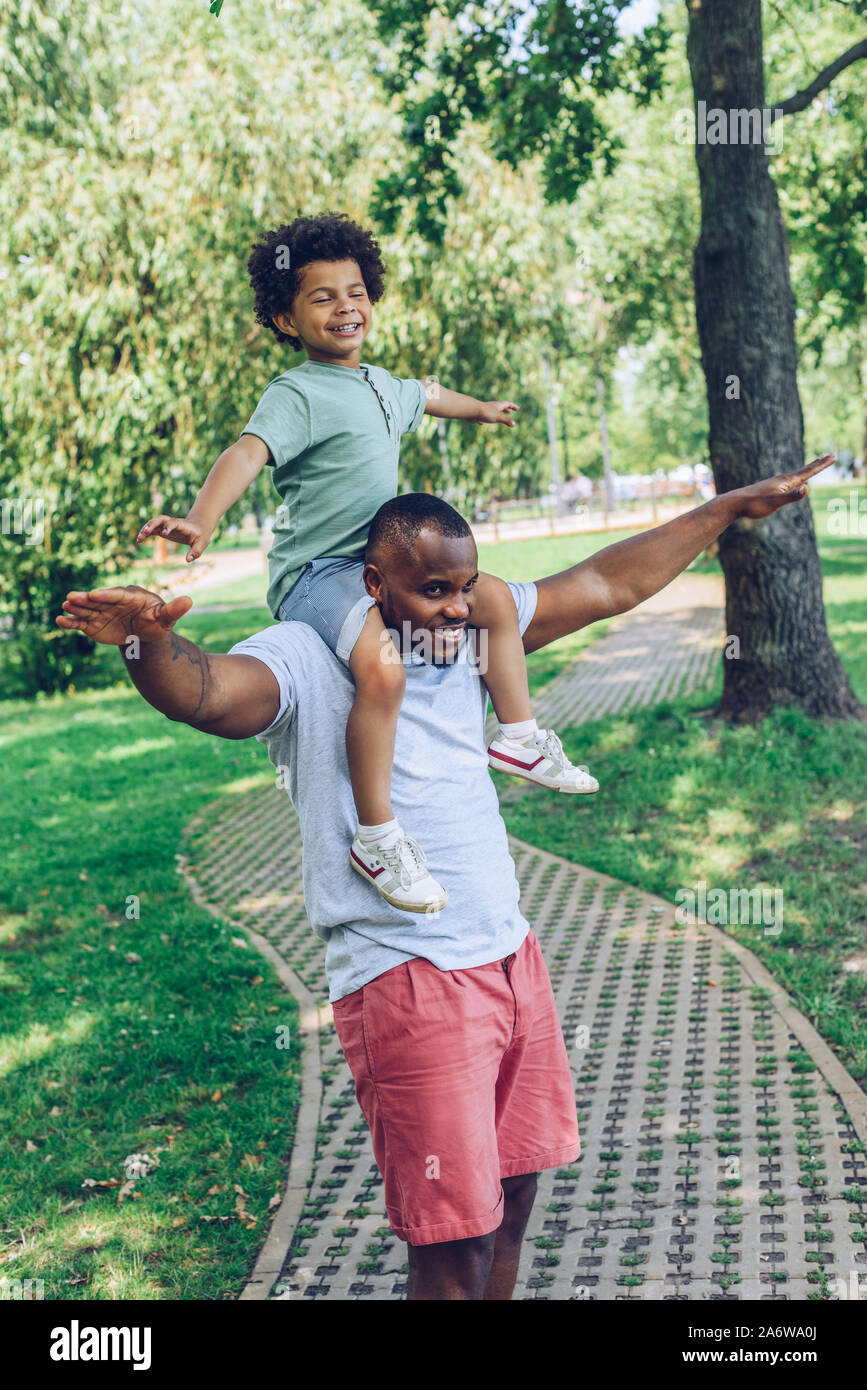 cheerful african american boy imitating flying while piggybacking with ...