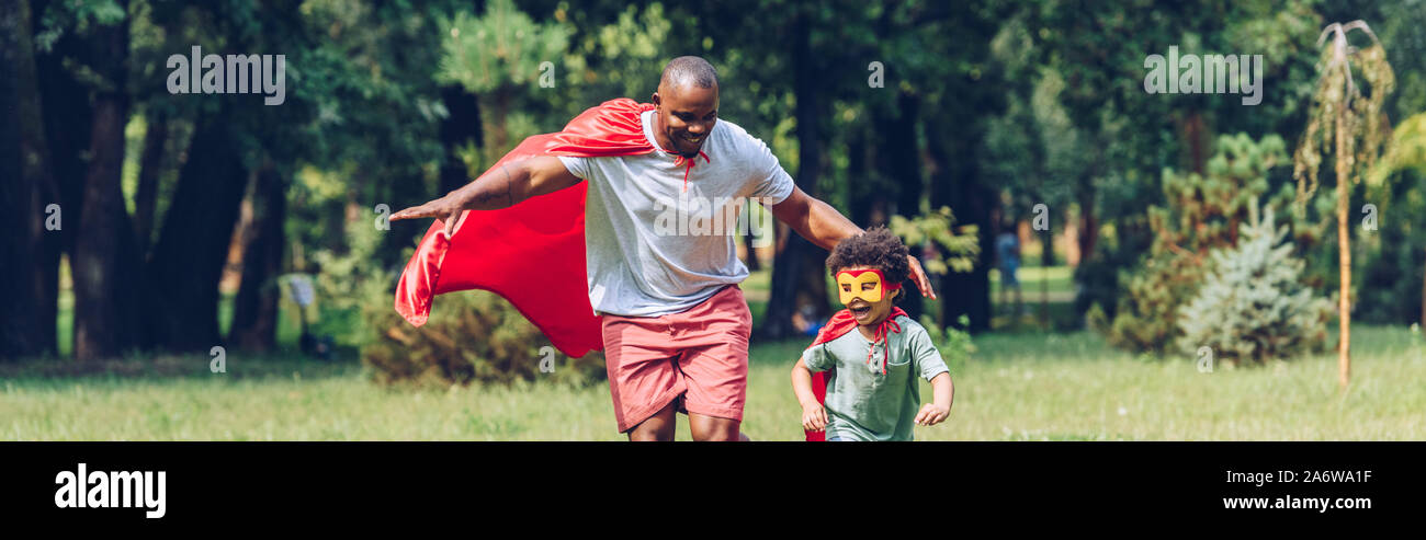 panoramic shot of african american father and son running in costumes ...
