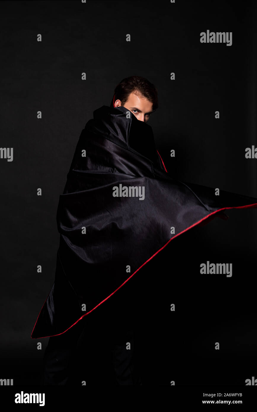 man covering face with cloak of halloween costume on black Stock Photo ...