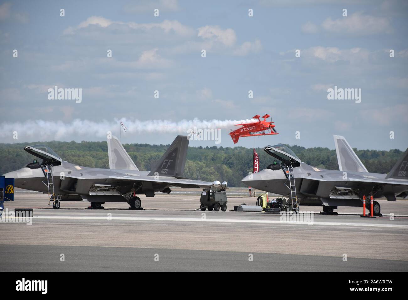 A station of fighter jets with two parked jets and one red plane flying ...