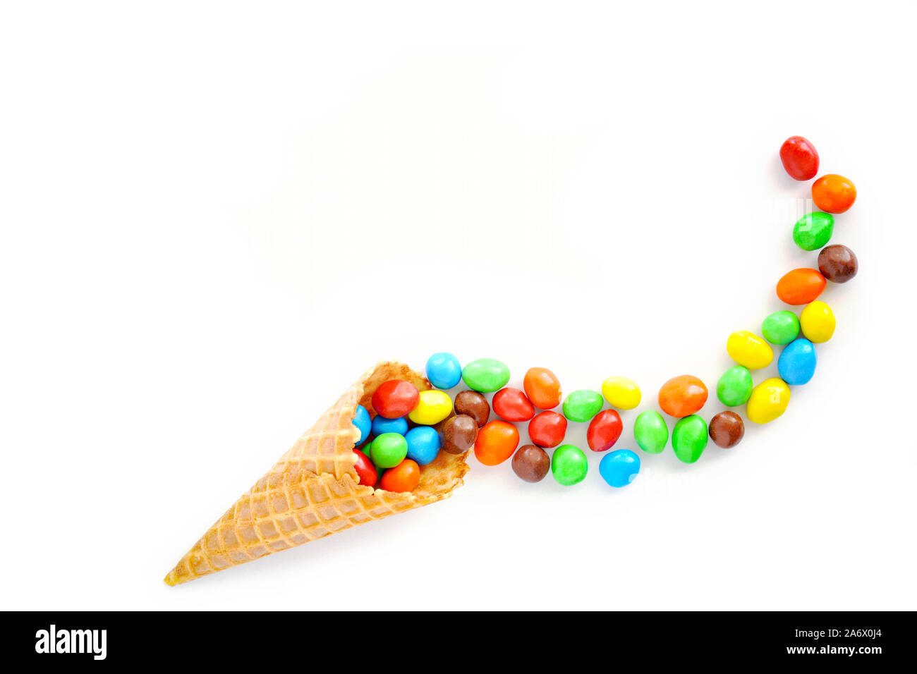 Colorful candy coated peanuts spilling from waffle cone on white ...