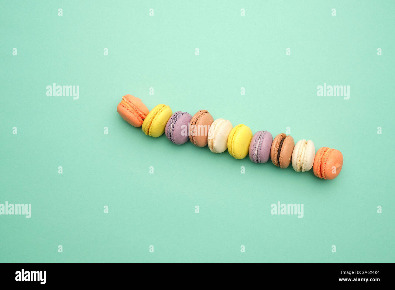 round multi-colored baked macarons with cream lie in a line on a green ...