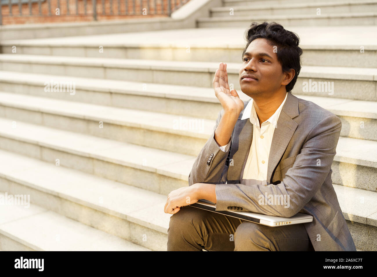Young handsome Indian man is sitting with a laptop, smiling and typing ...