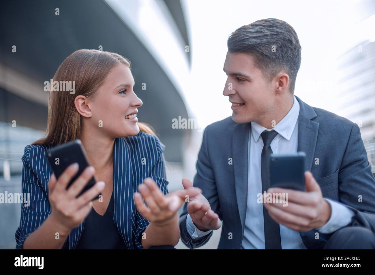 two young employees with smartphones sitting near office building Stock ...