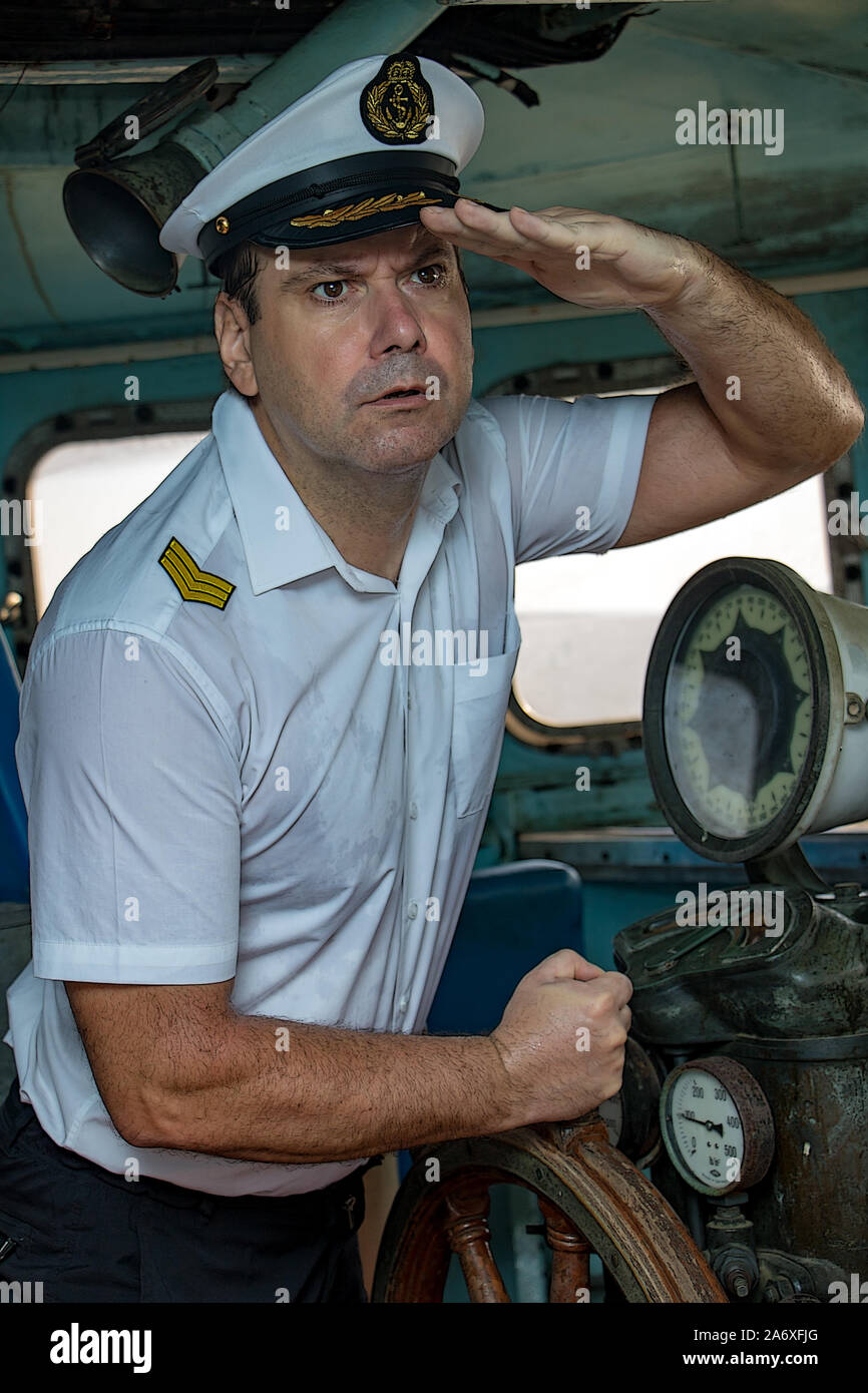 A sailor officer in the uniform is steering the ship with a rudder ...