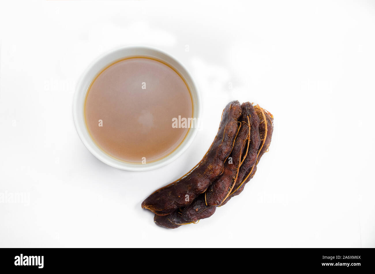 Fresh tamarind fruits brown and juice in a white cup on top view ...