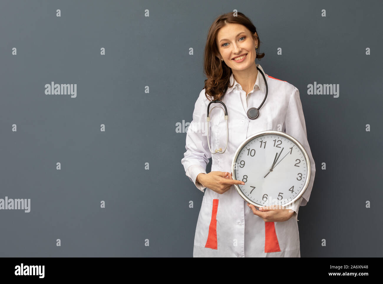 woman doctor smiles and shows big clock Stock Photo - Alamy
