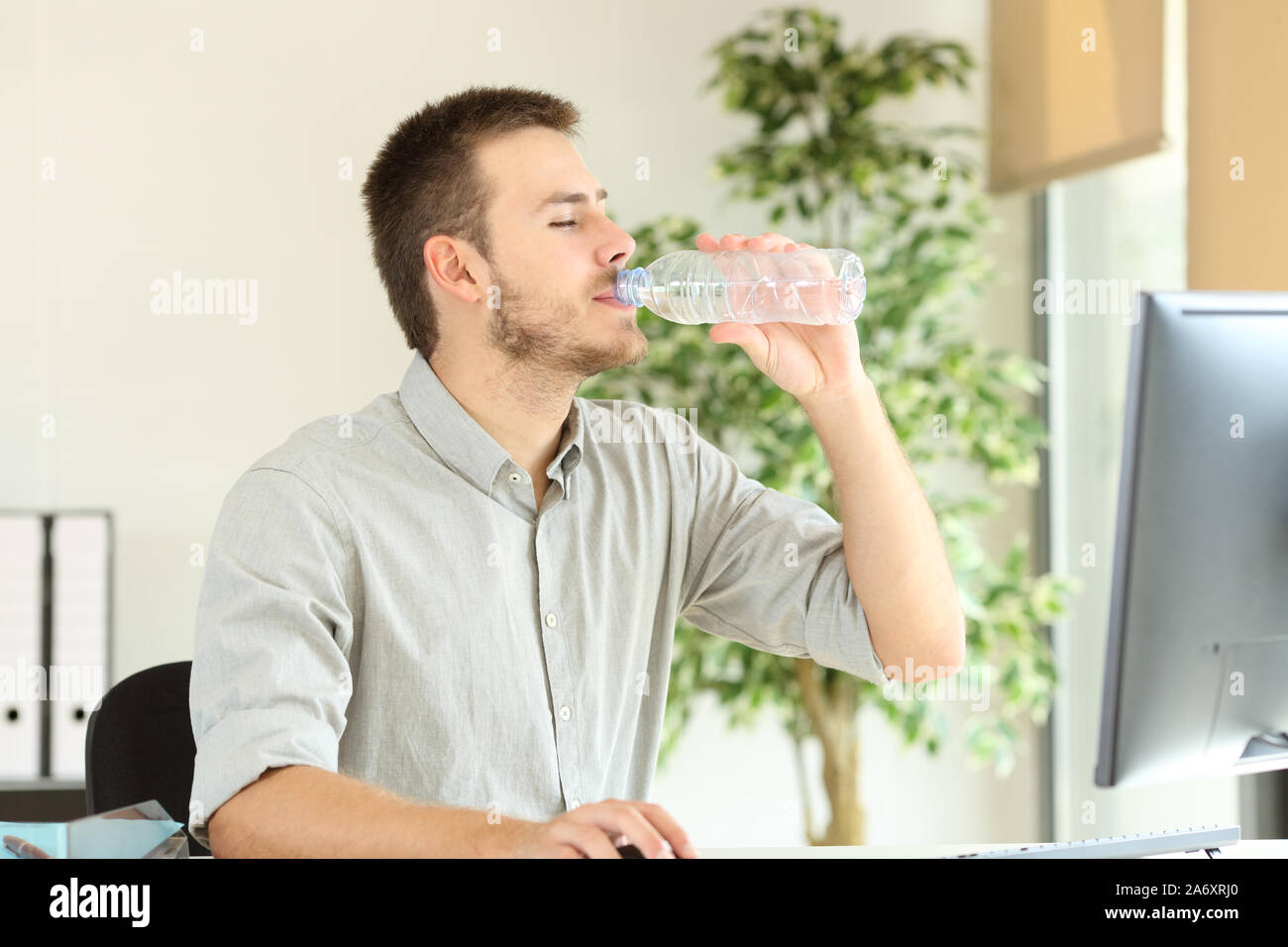 Office worker working and drinking bottled water sitting on a chair at ...