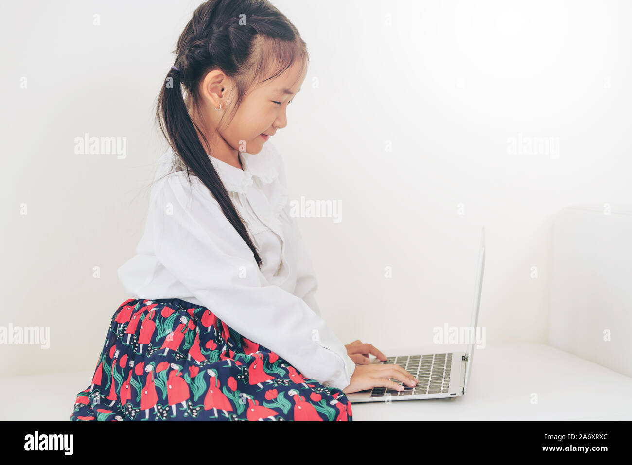 Little happy kid using laptop computer sitting on white sofa. Childhood ...