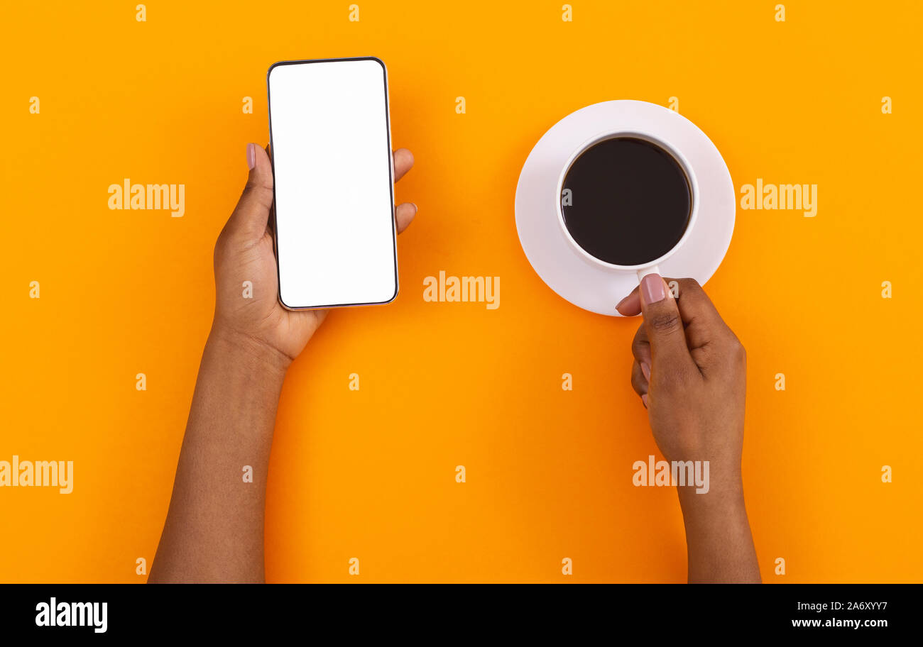 Black woman holding smartphone with blank screen and drinking coffee ...