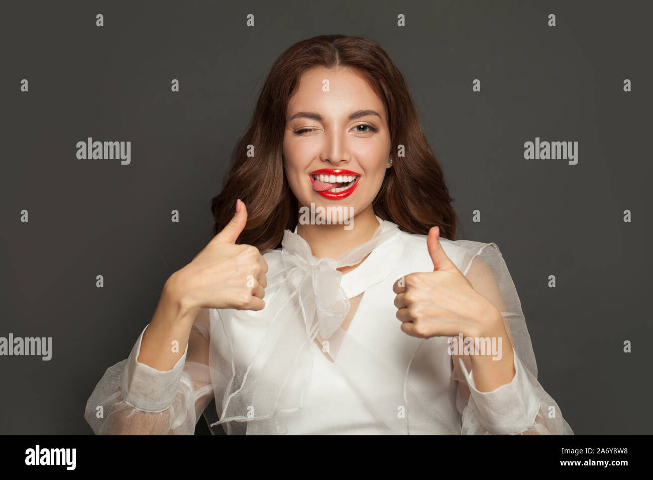 Beautiful funny woman winking, showing thumb up and tongue Stock Photo ...