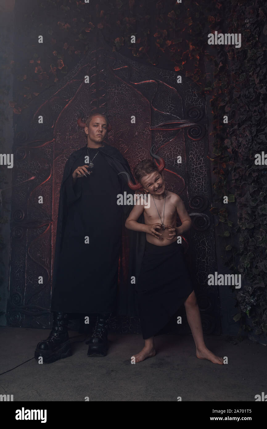 small child with red horns of demon and adult scary man standing in ...