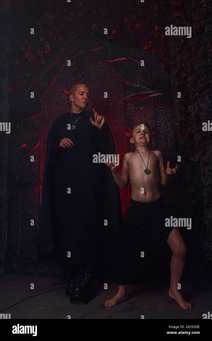 small child with red horns of demon and adult scary man standing in ...