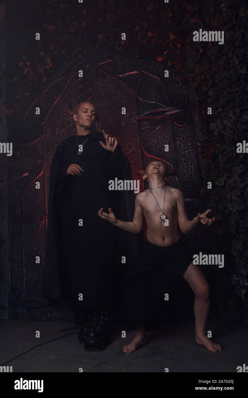 small child with red horns of demon and adult scary man standing in ...