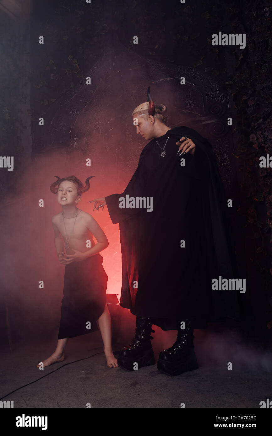 small child with red horns of demon and adult scary man standing in ...