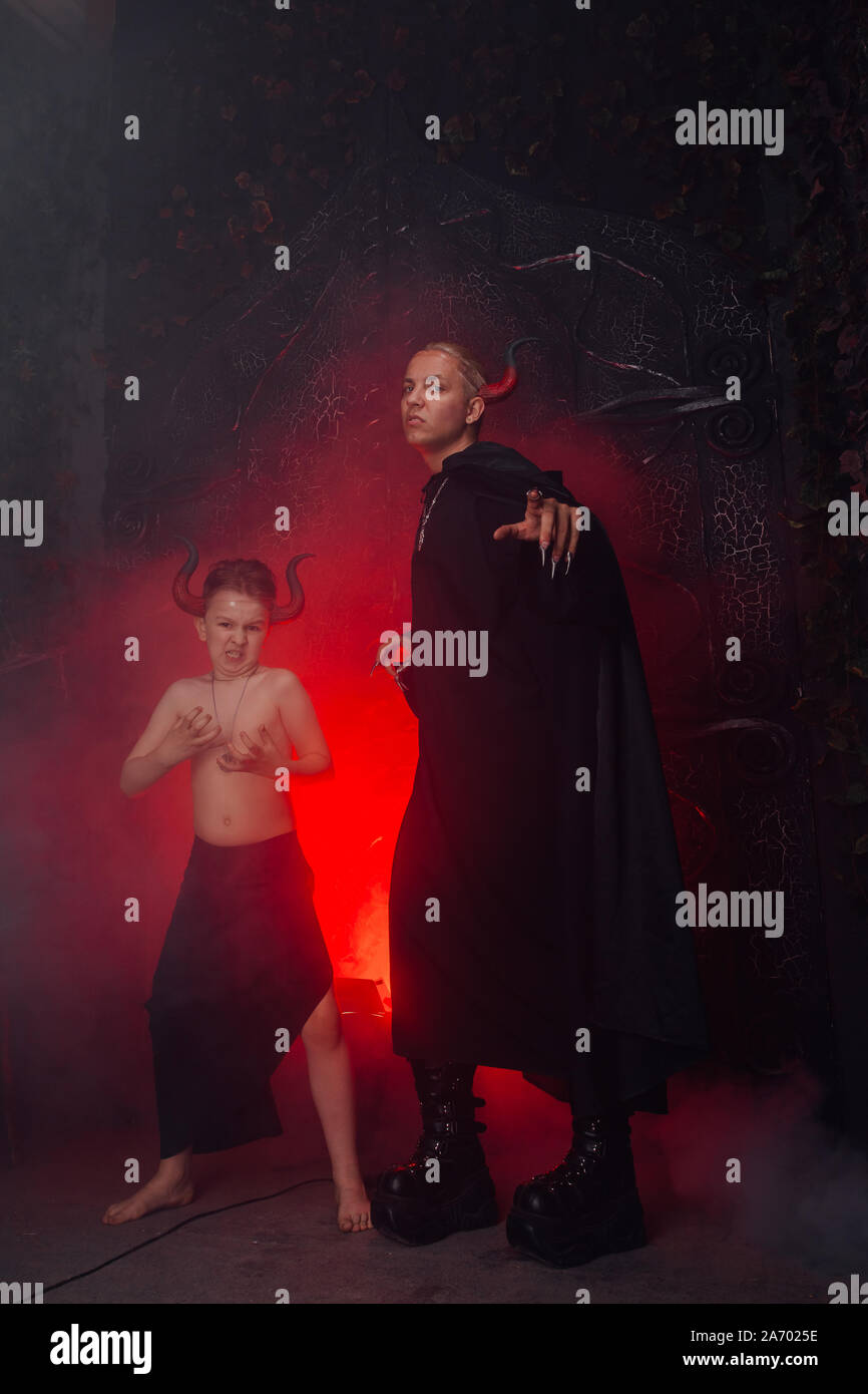 small child with red horns of demon and adult scary man standing in ...