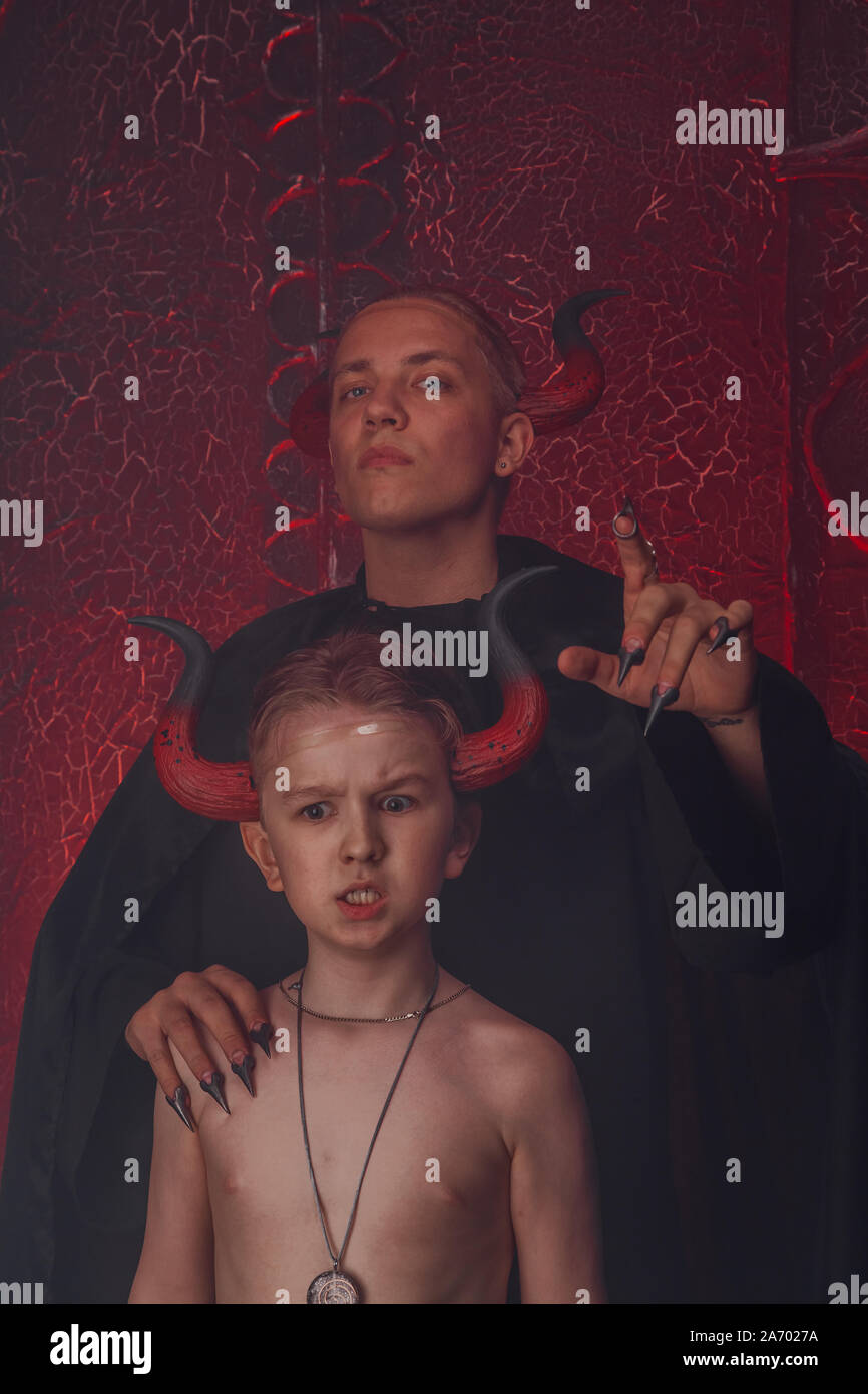 small child with red horns of demon and adult scary man standing in ...