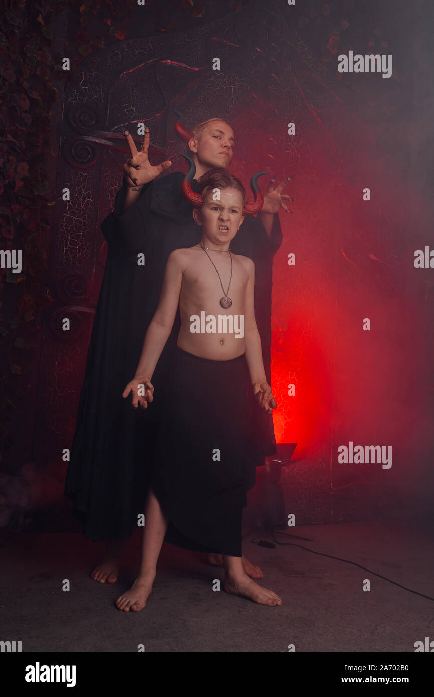 small child with red horns of demon and adult scary man standing in ...