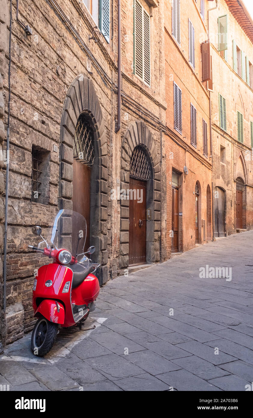 A bright red scooter is parked against a wall in a quiet side street of ...