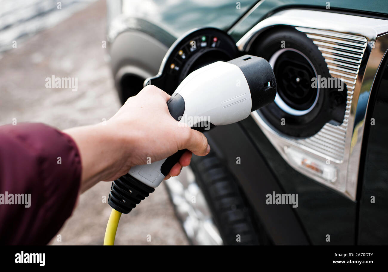 hand holding a lead towards an electric car socket Stock Photo - Alamy