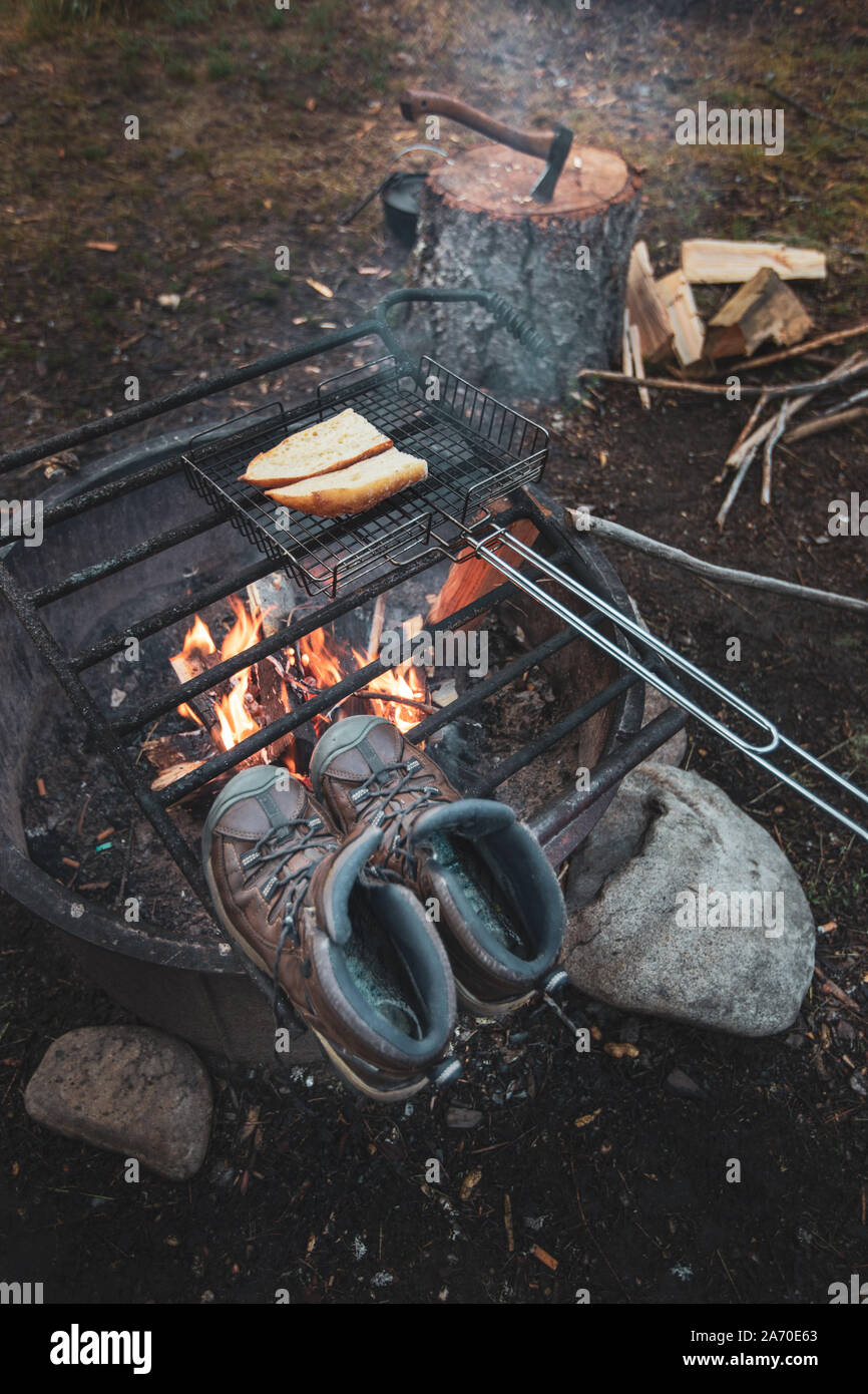 Wet hiking shoes drying by a campfire with bread toasting over the ...