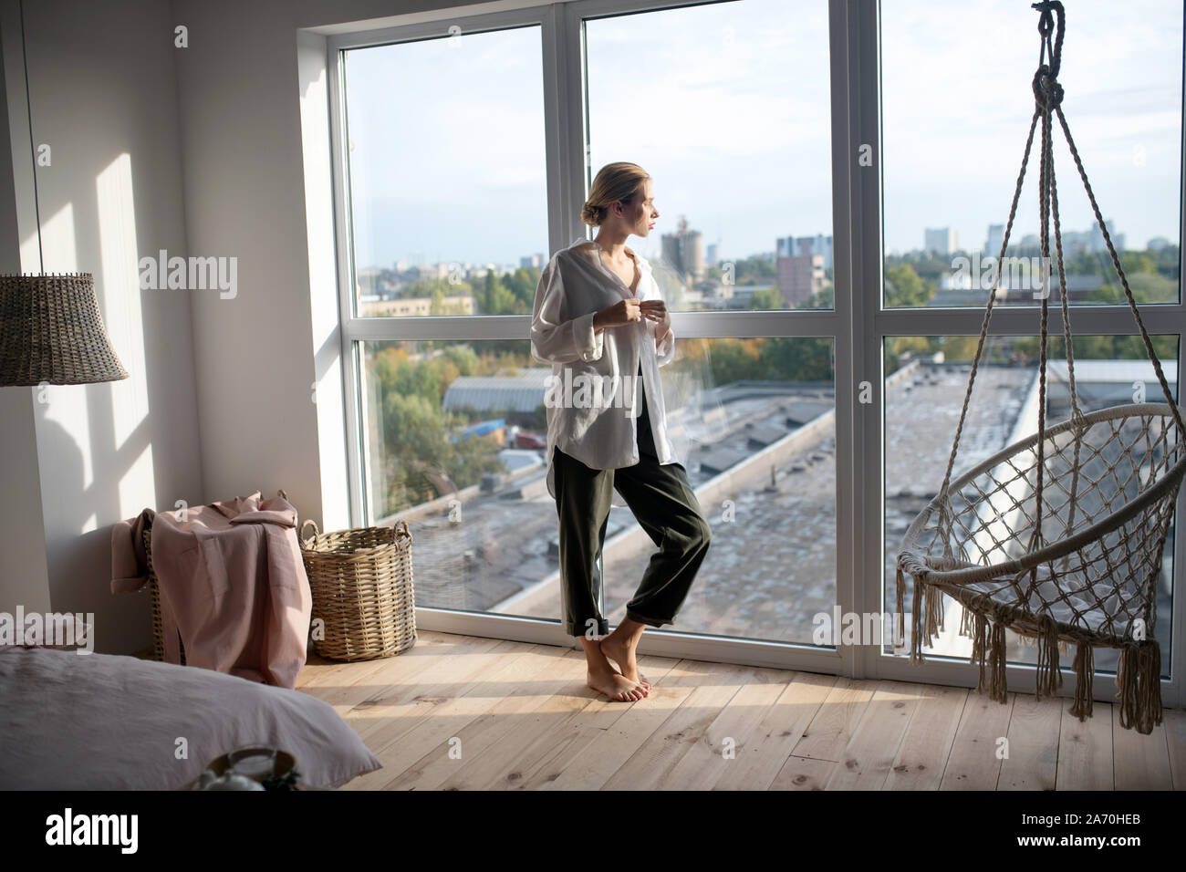 Blonde woman standing near window in living room Stock Photo - Alamy