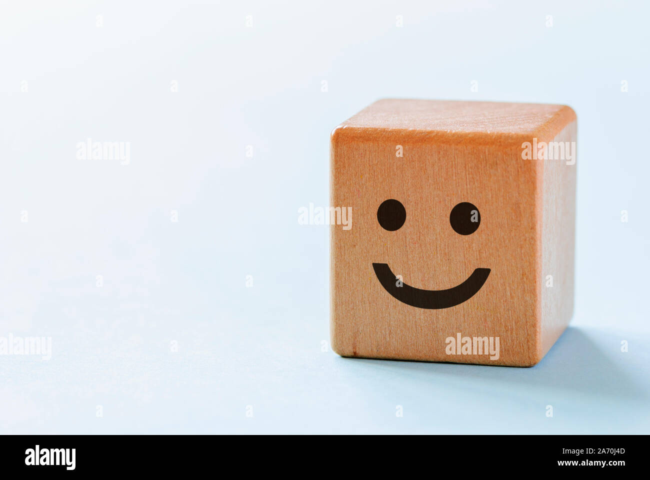 Wooden dice with happy smiley face emotion on the side, viewed in close ...