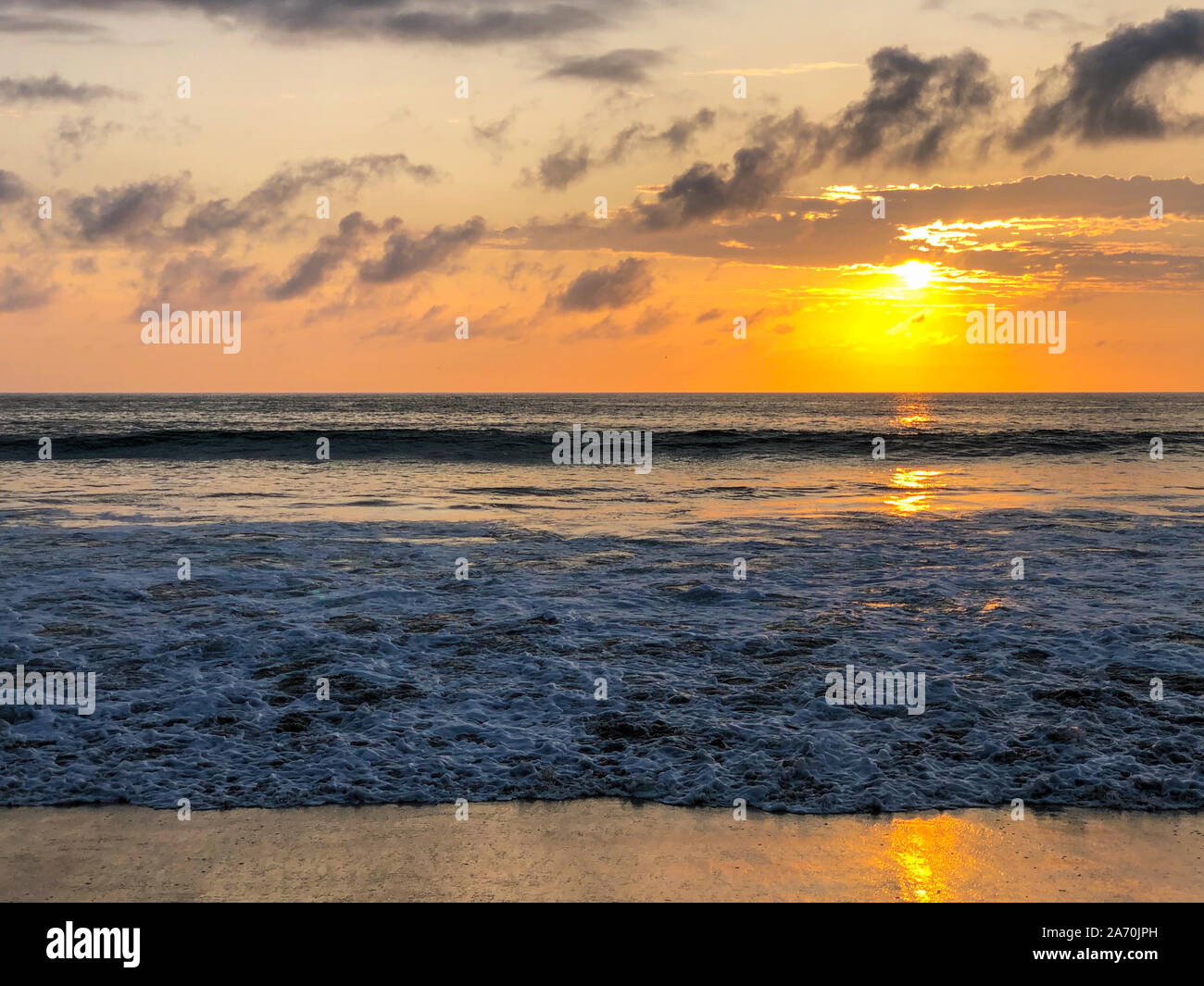 Colorful ocean beach sunset facing the sun with deep clouded sky ...