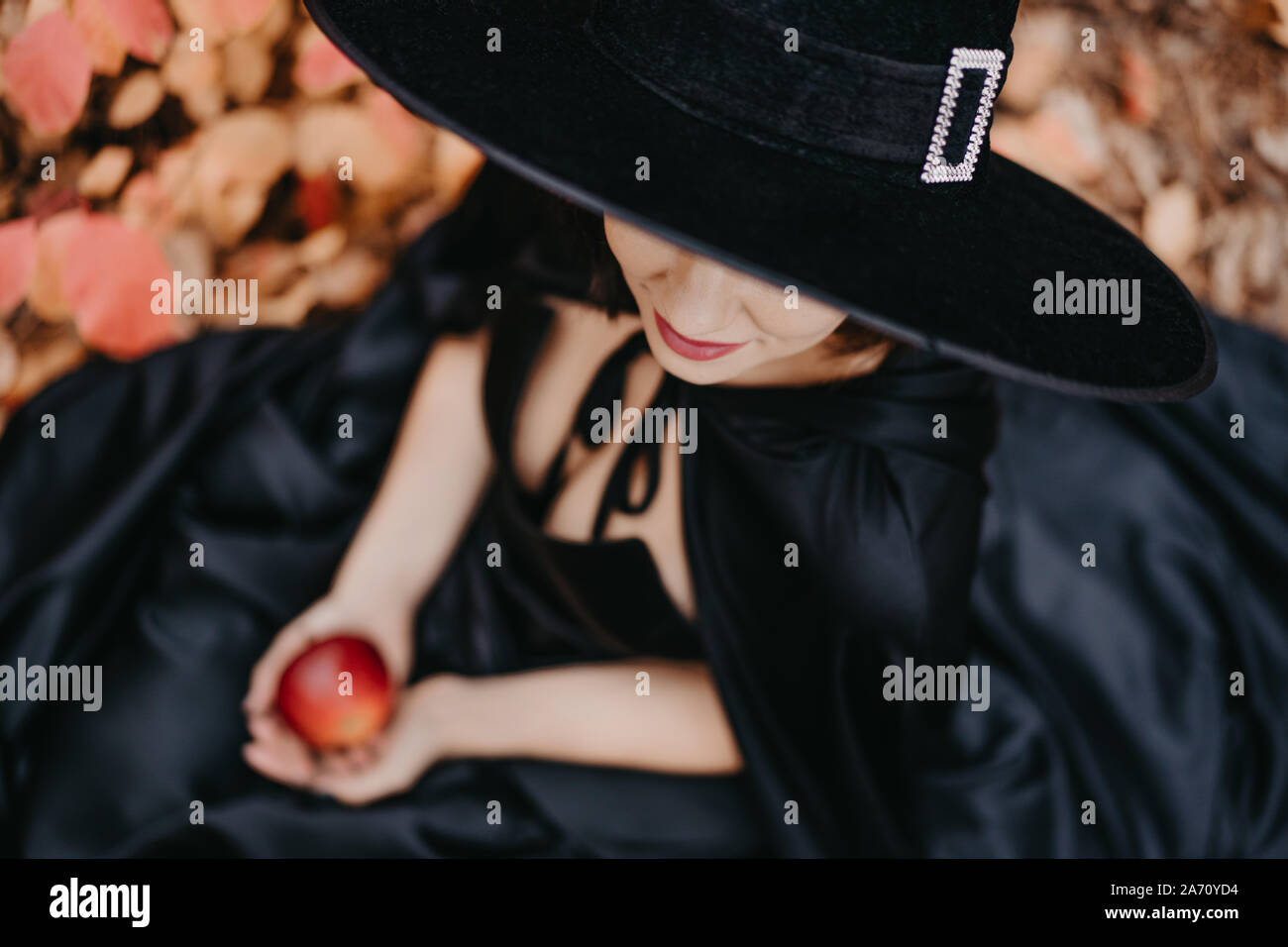 Unrecognizable girl as witch in black hat holding red apple as symbol ...