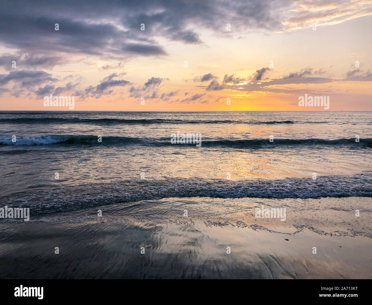 Colorful ocean beach sunset facing the sun with deep clouded sky ...