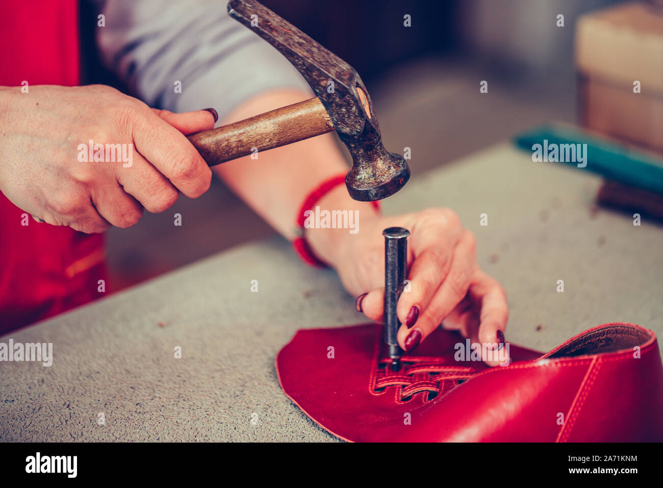 Close up of a female shoemaker working with leather using hammer and ...